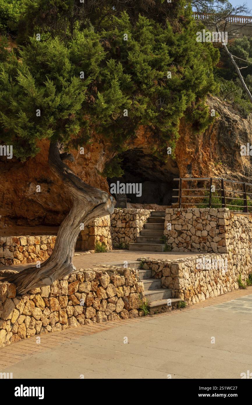 Stone stairs leading to a small cave in the rock face, shaded by a ...
