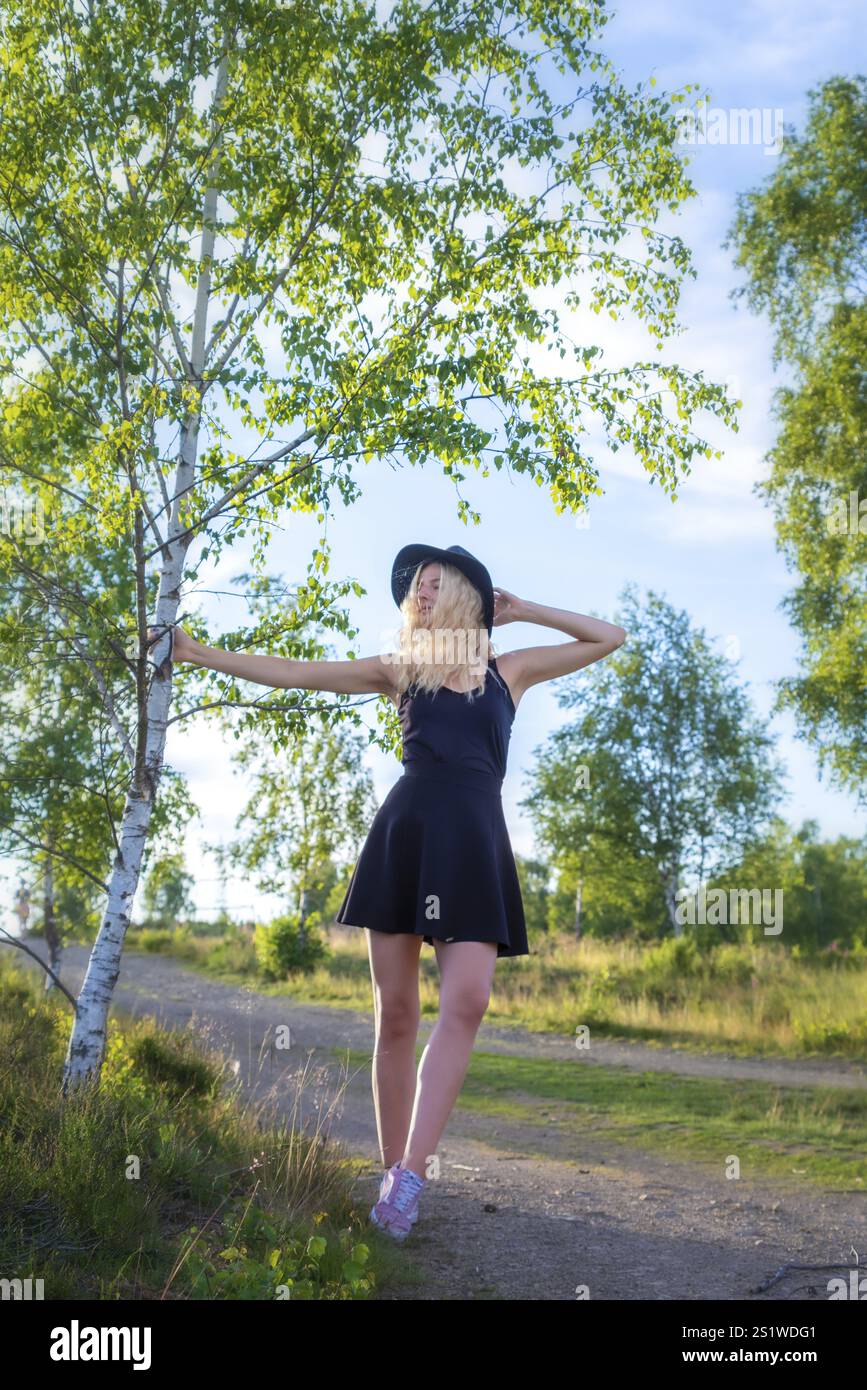 Young blonde Woman Standing beside a birch tree in nature with a ...