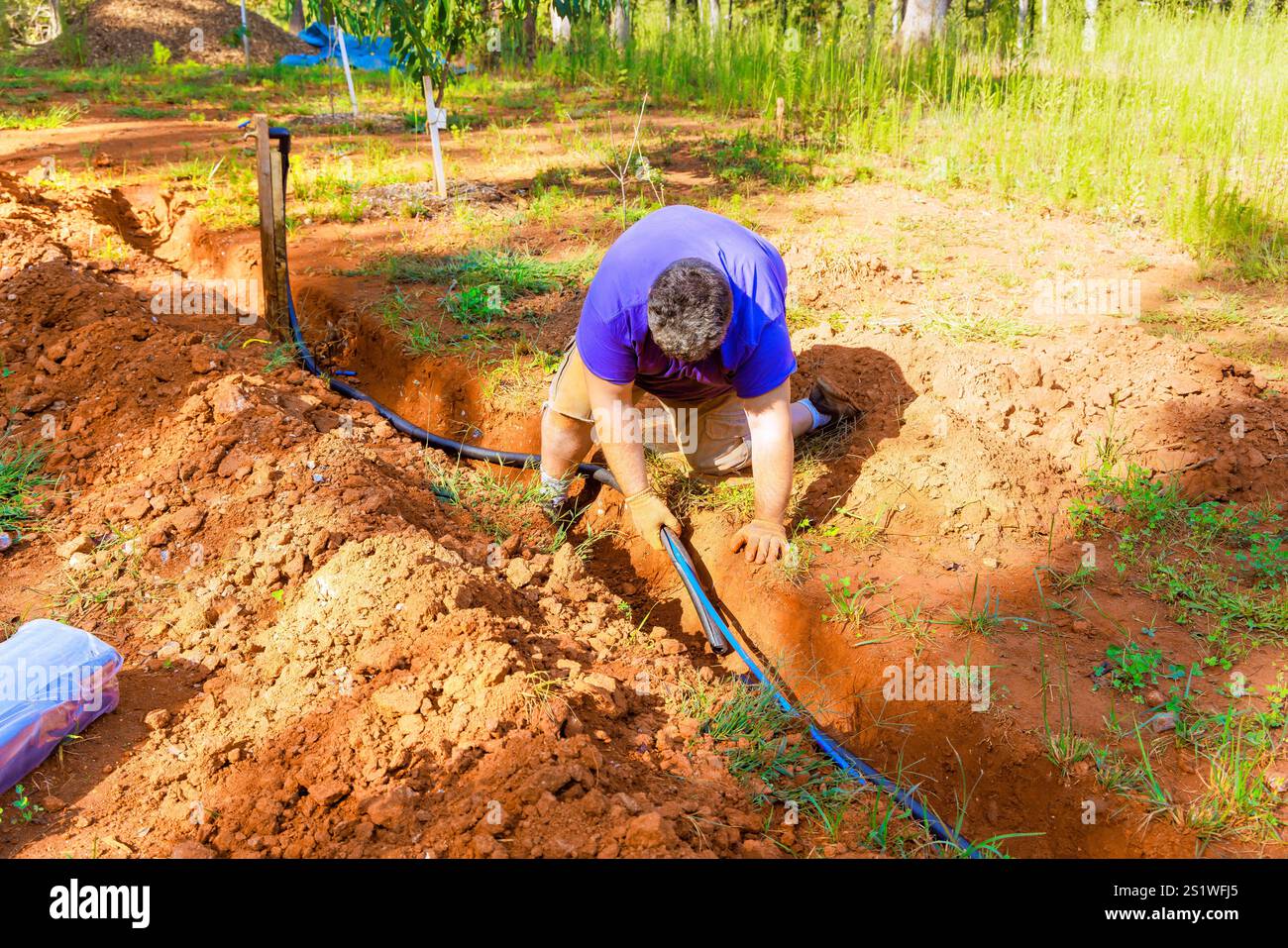 Worker in garden, digging, installing PVC water pipe for new irrigation ...