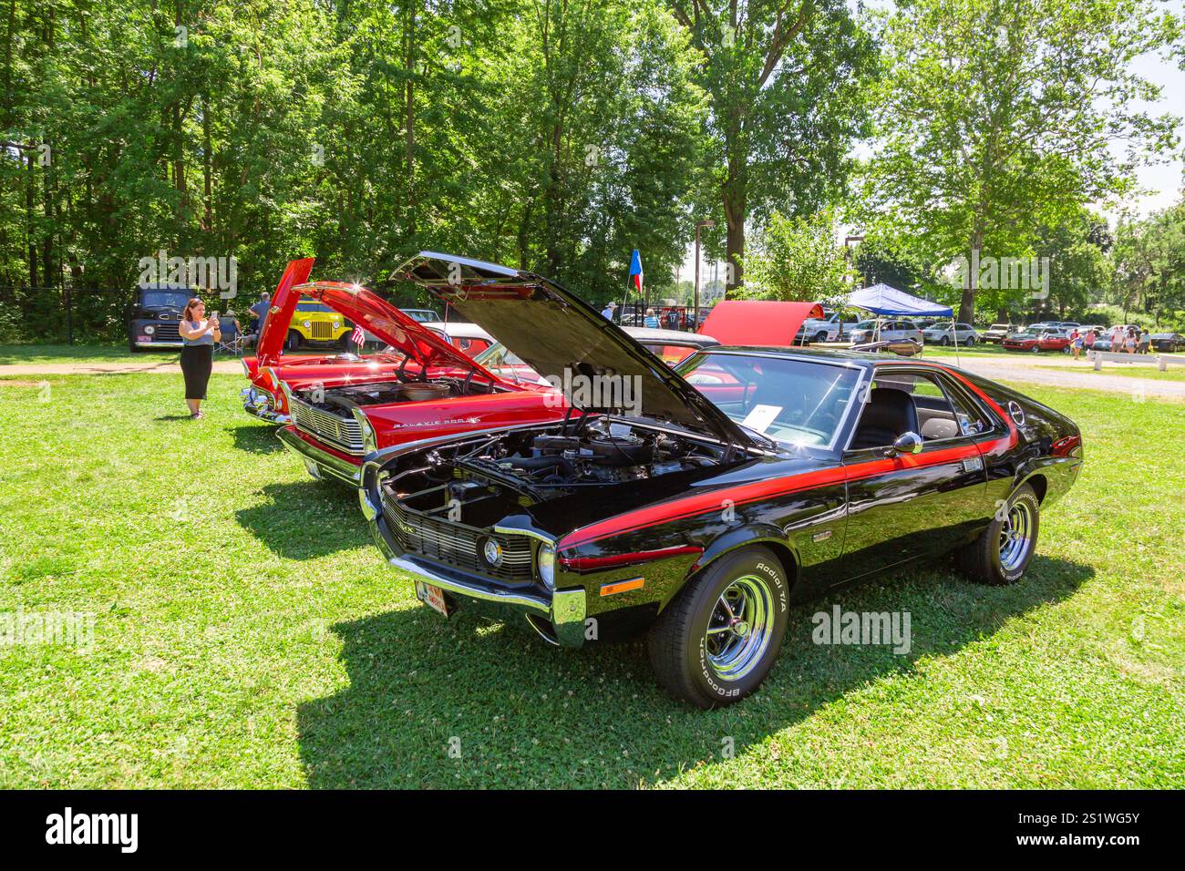 A black and red 1970 AMC AMX coupe parked in the grass at a car show in ...
