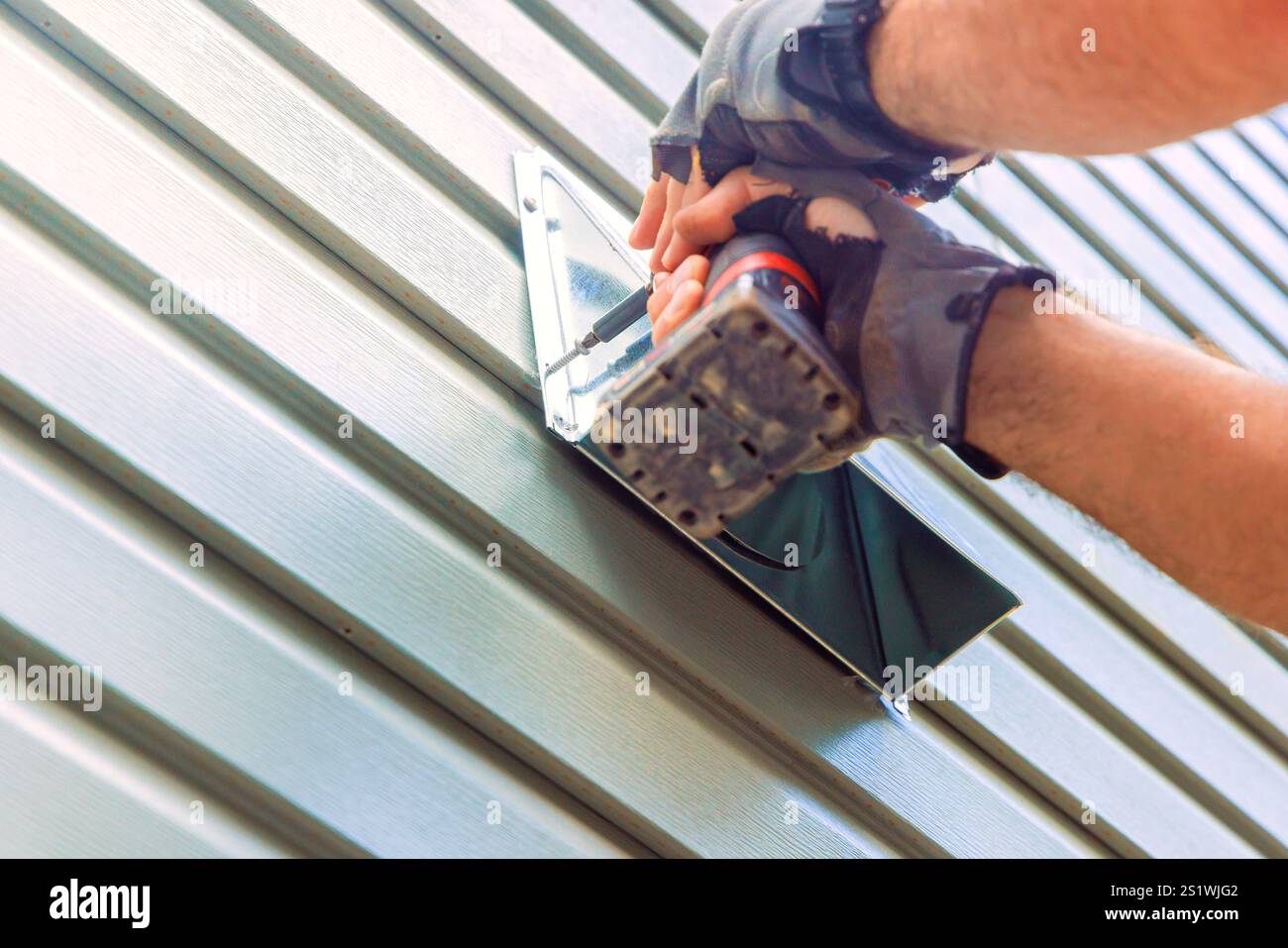 Contractor carefully secures metal vent cover fixture onto siding ...