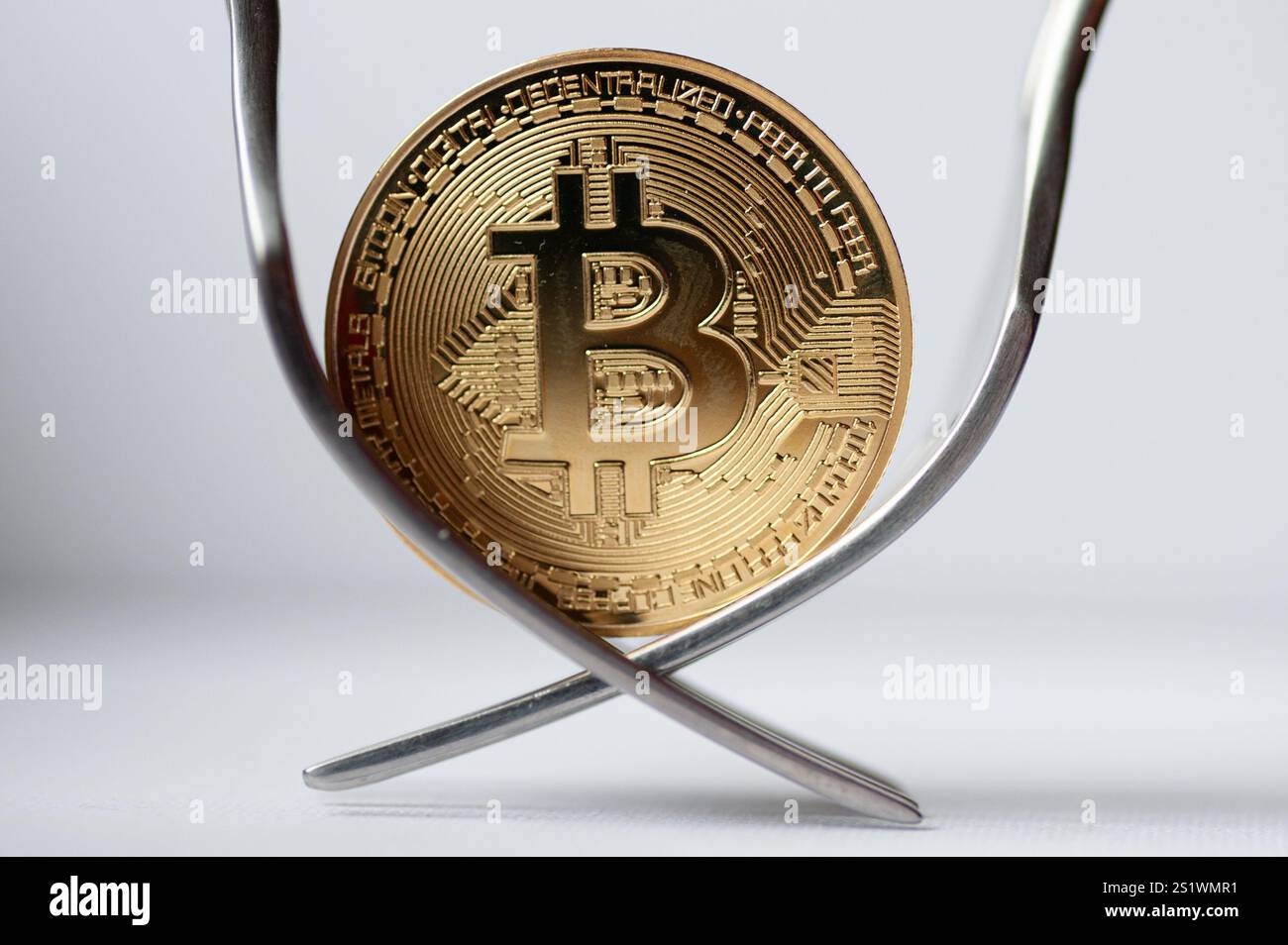 A coin with the letter Bitcoin on it is sitting on a fork. The fork is ...