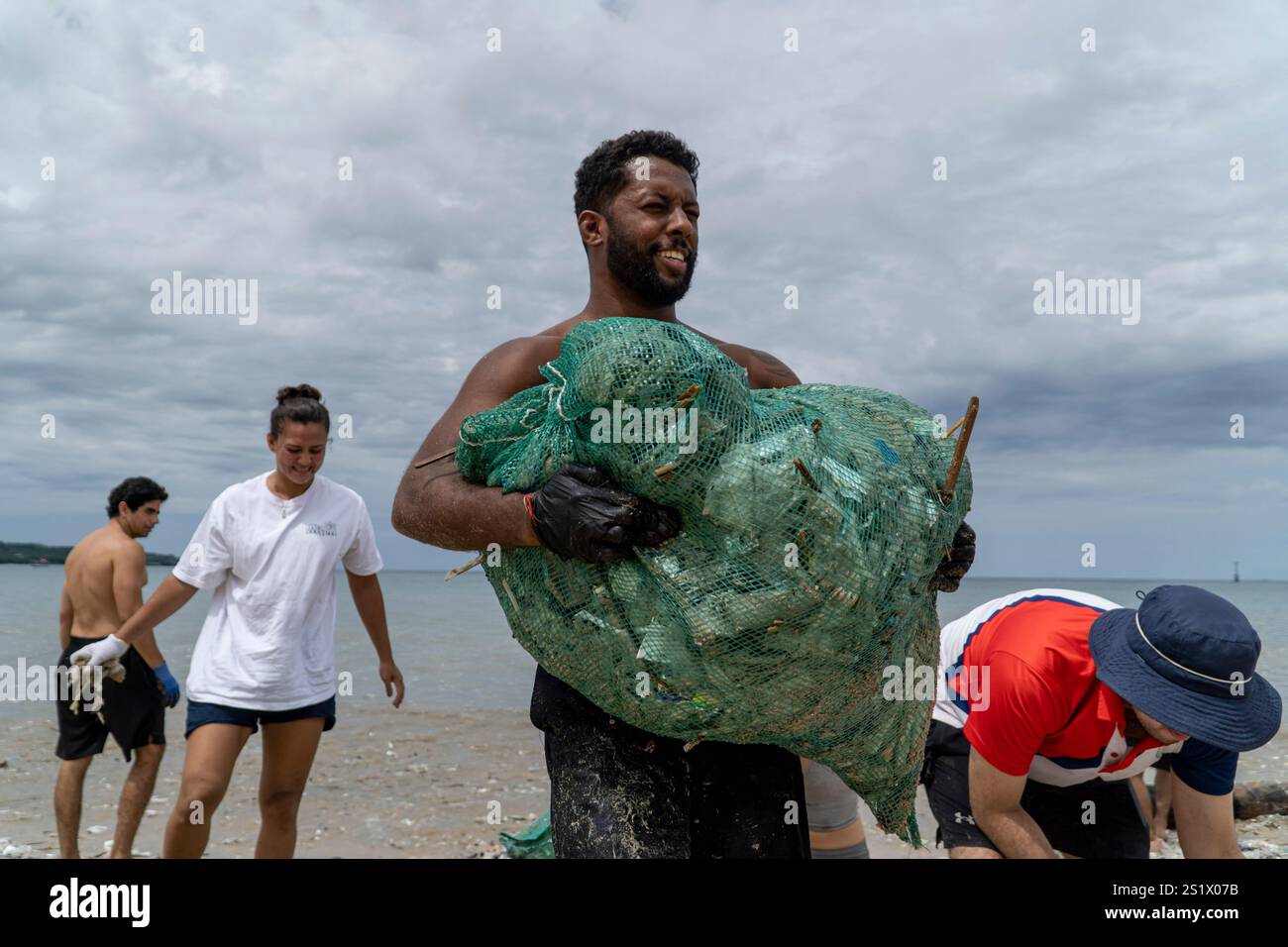 A volunteer carries a sack of trash washed ashore by seasonal monsoon ...