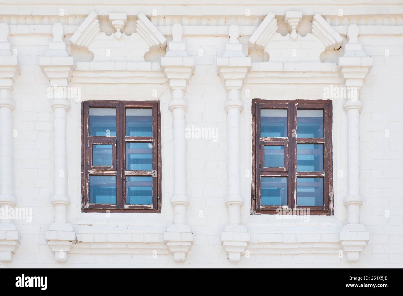 Two historic wooden windows in white brick facade. Decorative columns ...