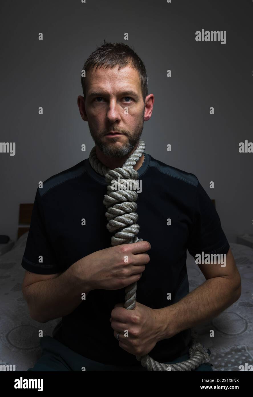 Depressed man sitting on bed with rope around neck. Suicide, mental ...