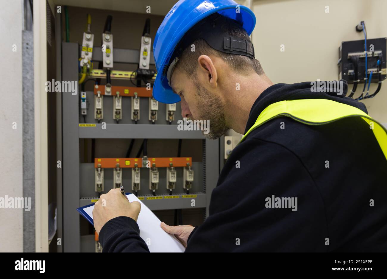 Worker in helmet and warning vest control circuit breaker, writing on ...
