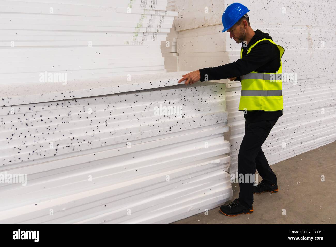 A worker wearing a helmet and safety vest stacks polystyrene panels ...