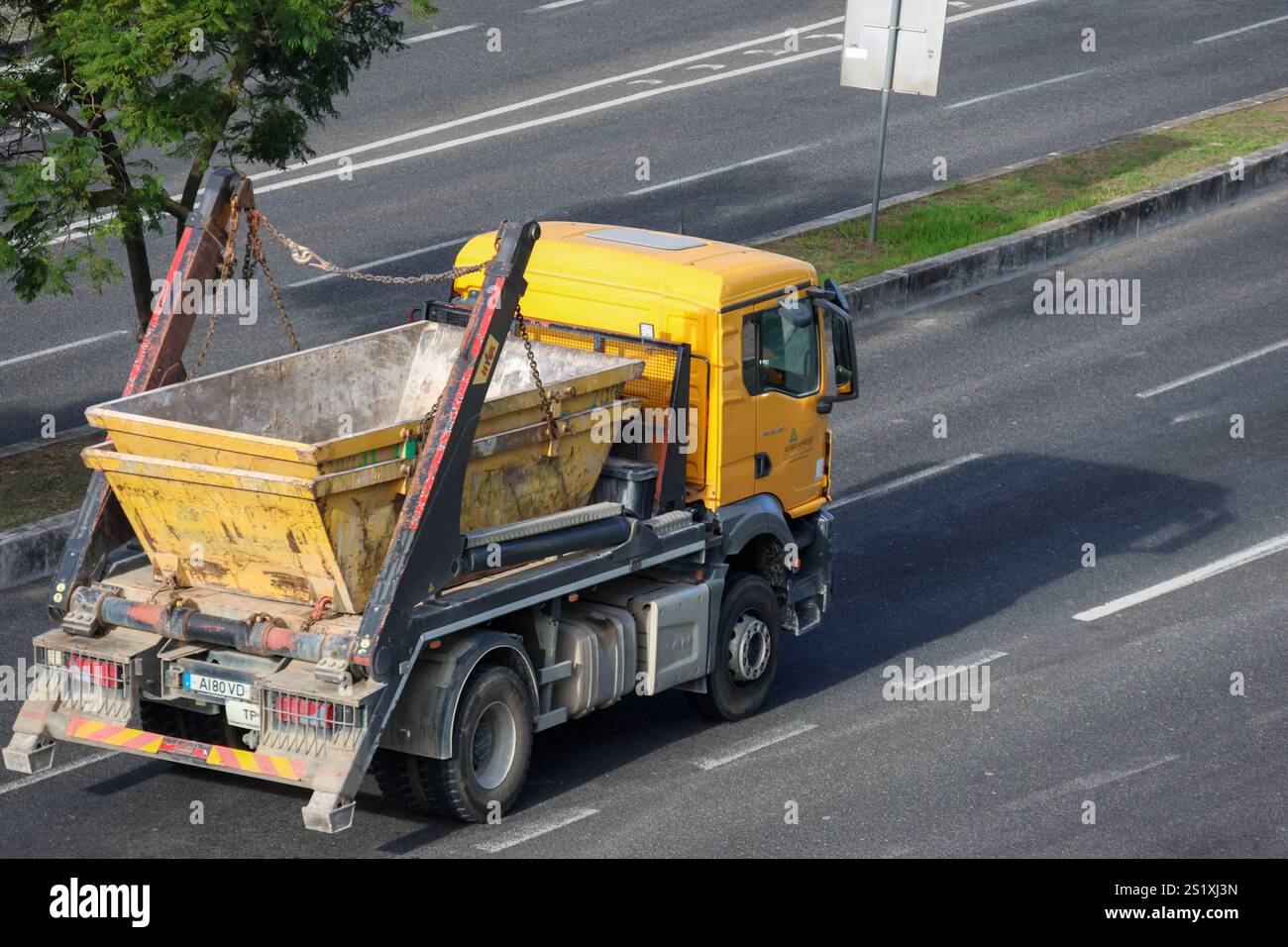 Yellow skip loader truck carrying a metal waste container driving on a ...