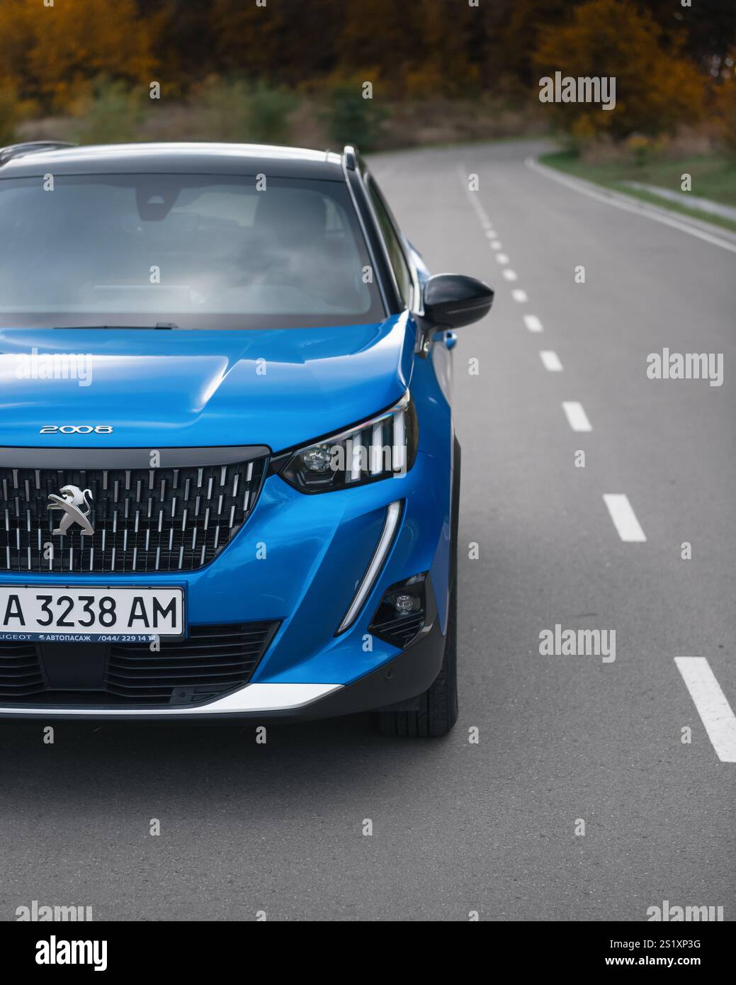 Blue Peugeot 2008 on a road in autumn forest. Close-up front view of ...
