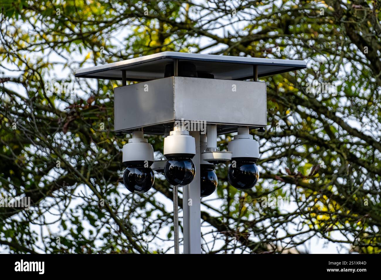 four cctv cameras on metal light pole, blue sky and green tree ...