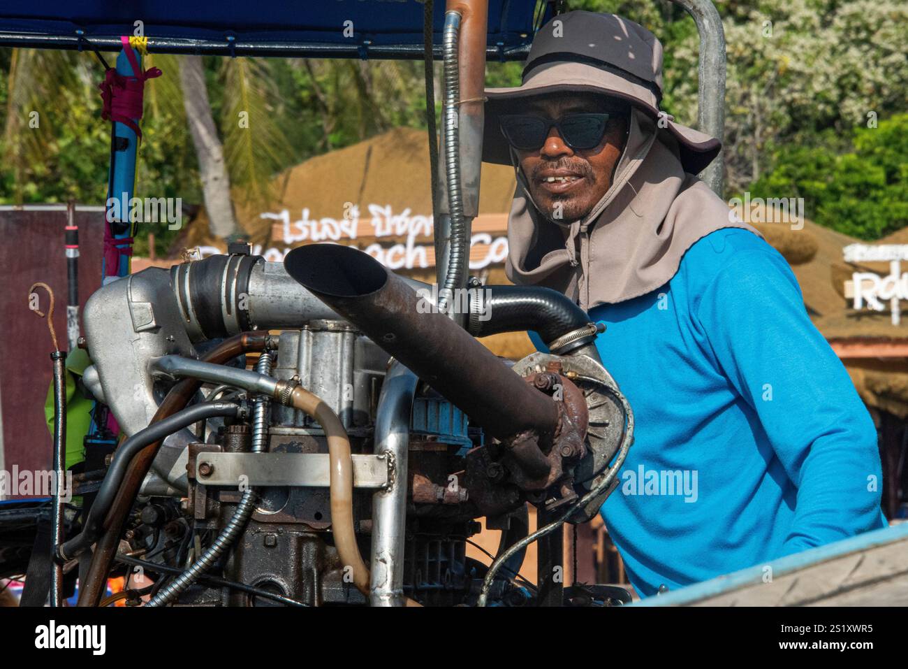 Thai longtail boat operator wearing a blue shirt and sun hat ...