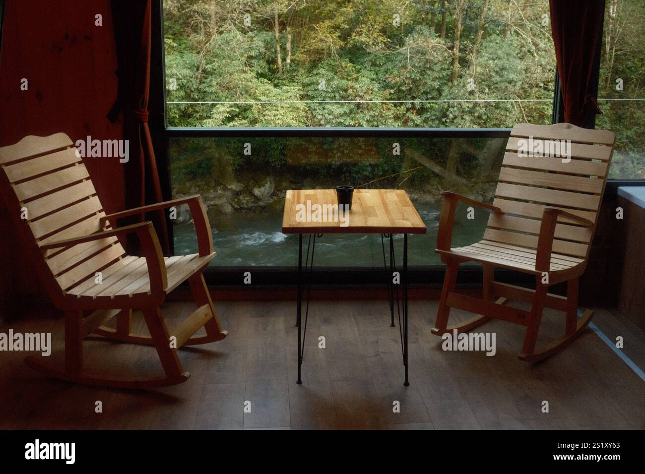 Wooden rocking chairs and small table facing a large glass window with ...
