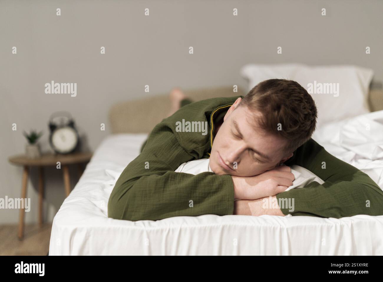 Man is sleeping on a bed. There is a clock on the left side of the bed ...