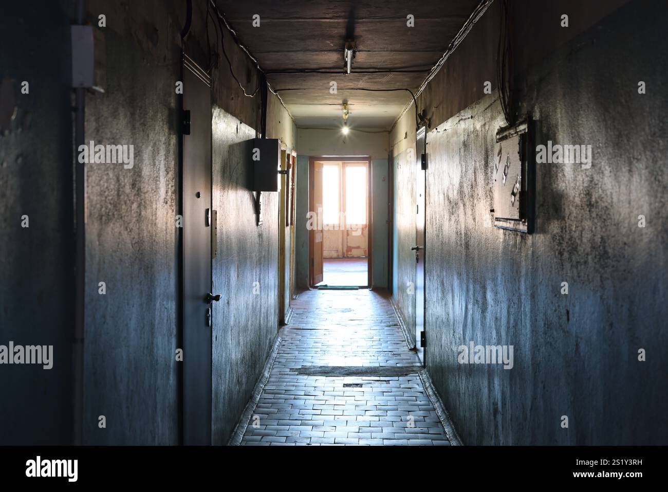 A dimly lit corridor stretches ahead, leading to an open doorway that ...