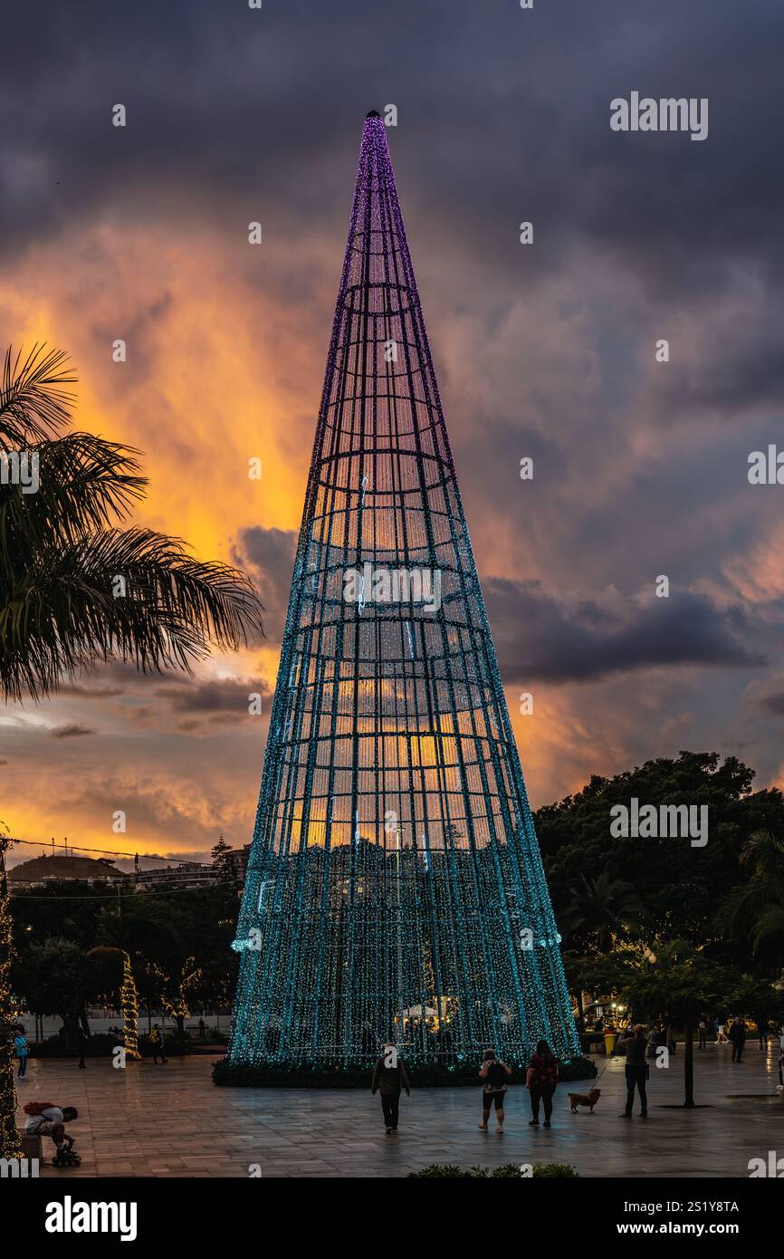 A tall, luminous Christmas tree sculpture glowing in a park as vibrant ...