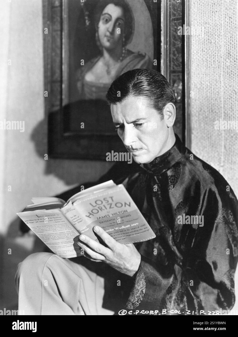 RONALD COLMAN in costume for his role as Robert Conway looks at a copy ...