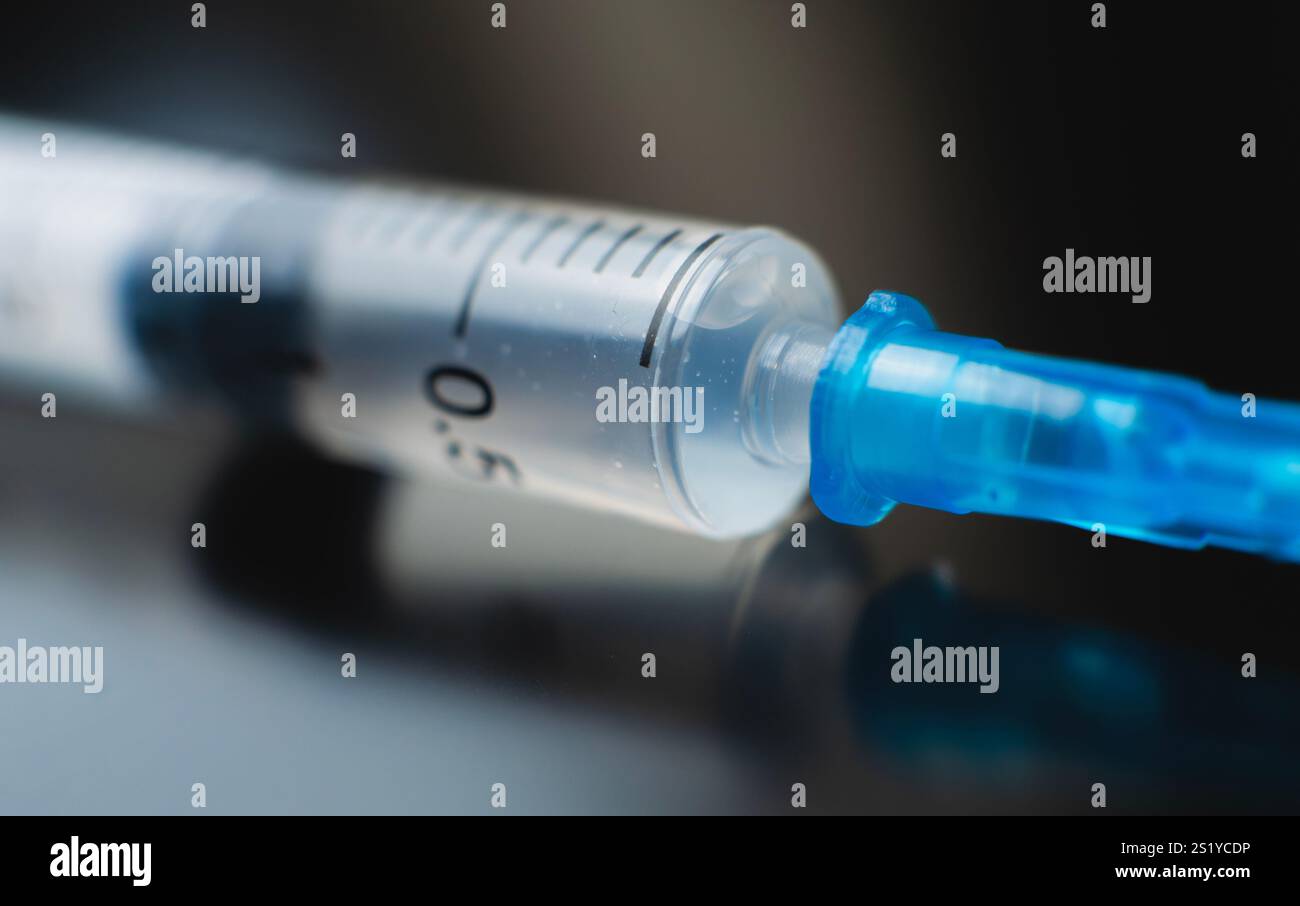 Syringe filled with liquid positioned on a dark surface in a healthcare ...