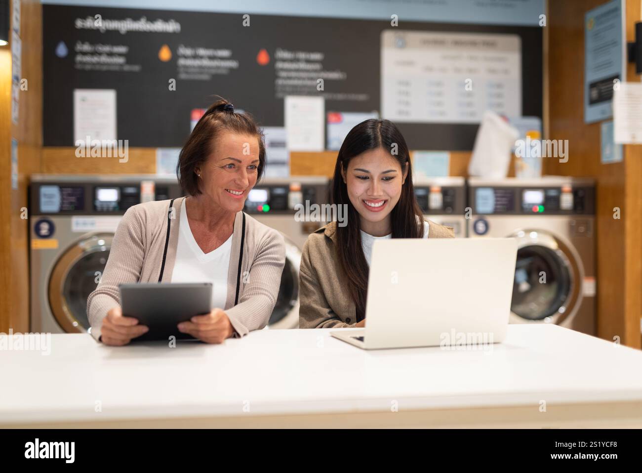 Two women working on a computer in laundry shop concept Stock Photo - Alamy