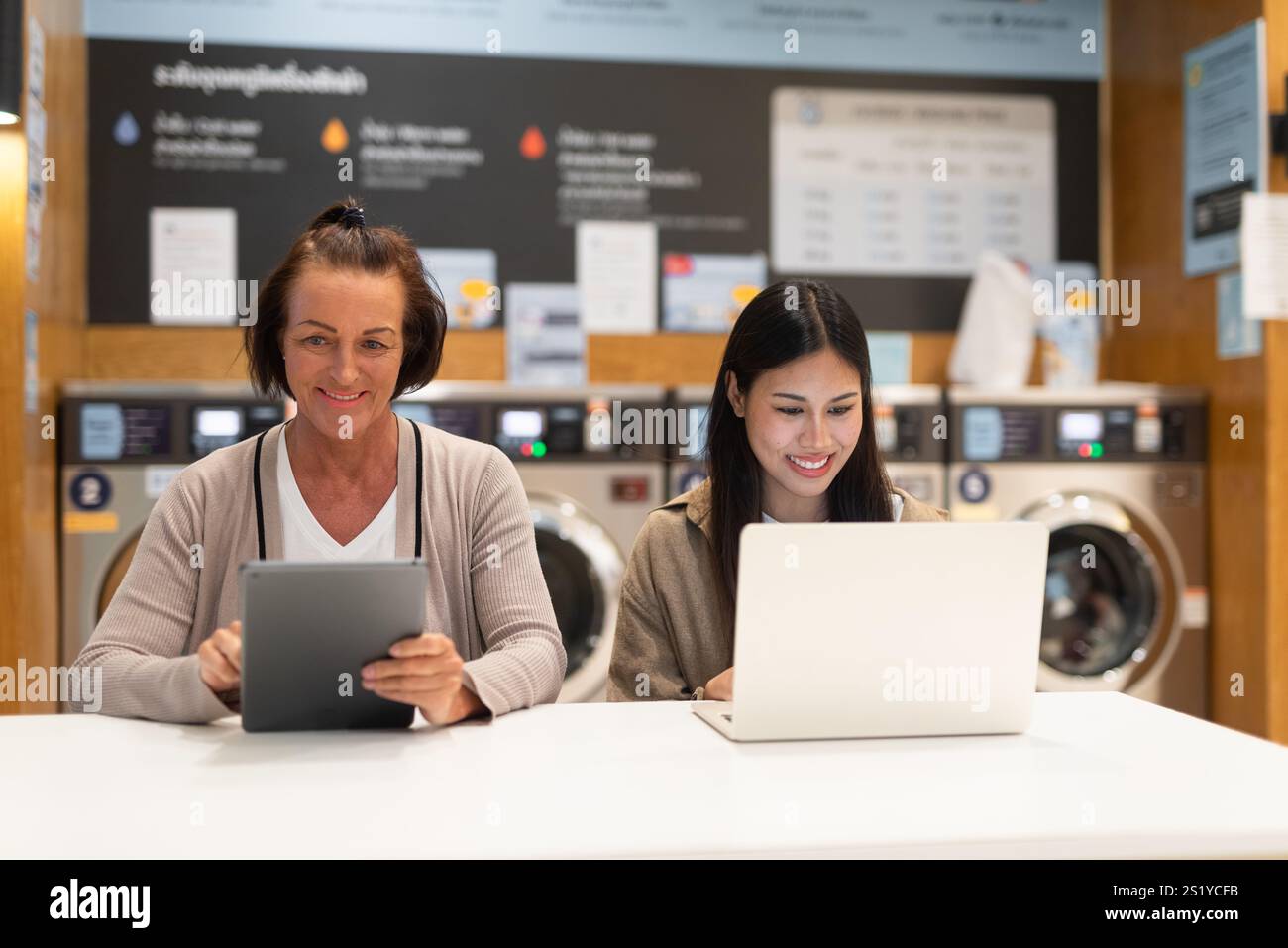 Two women working on a computer in laundry shop concept Stock Photo - Alamy
