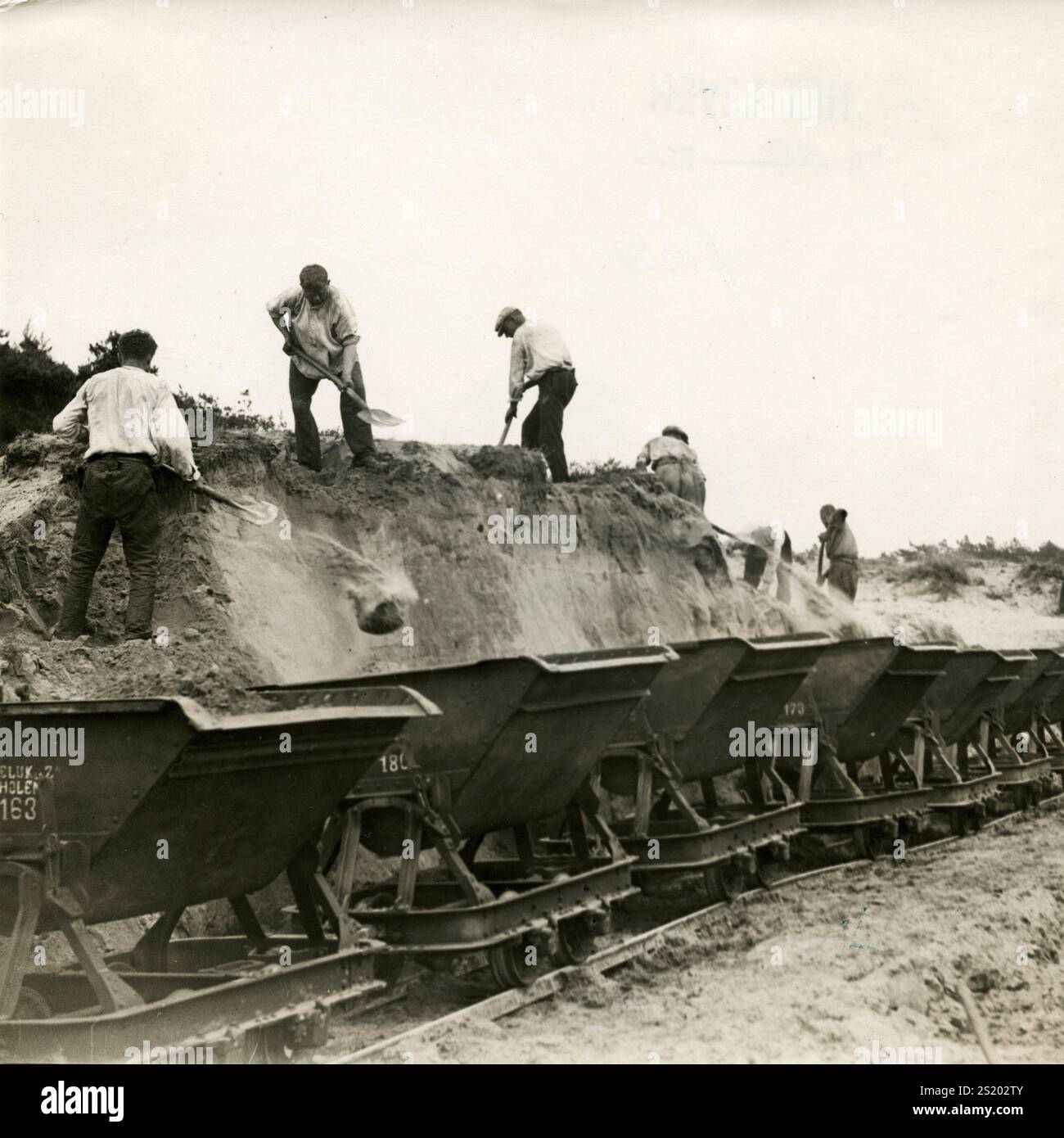 Workers shovel sand into carts on a rail. Road construction across the heath. Laren NH ...