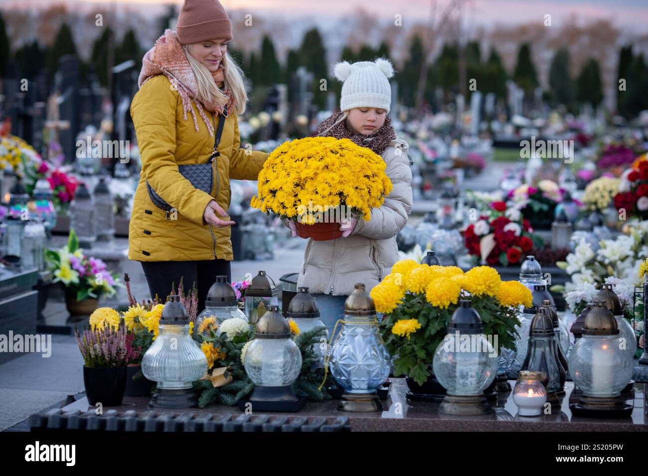A woman and a child visit a peaceful cemetery with bright yellow flowers to honor their late ...