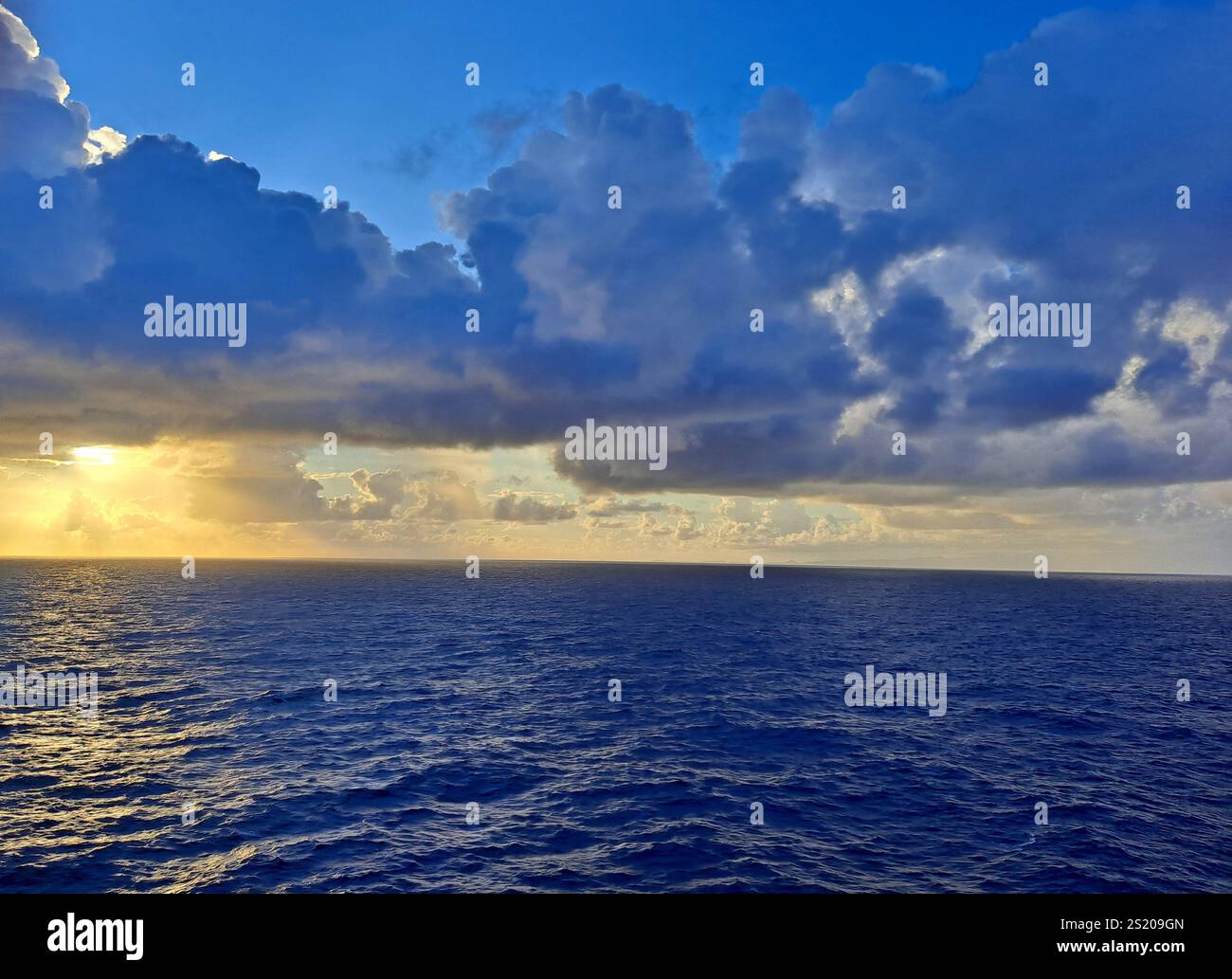 The sun setting over the Caribbean Ocean with fluffy clouds and blue ...
