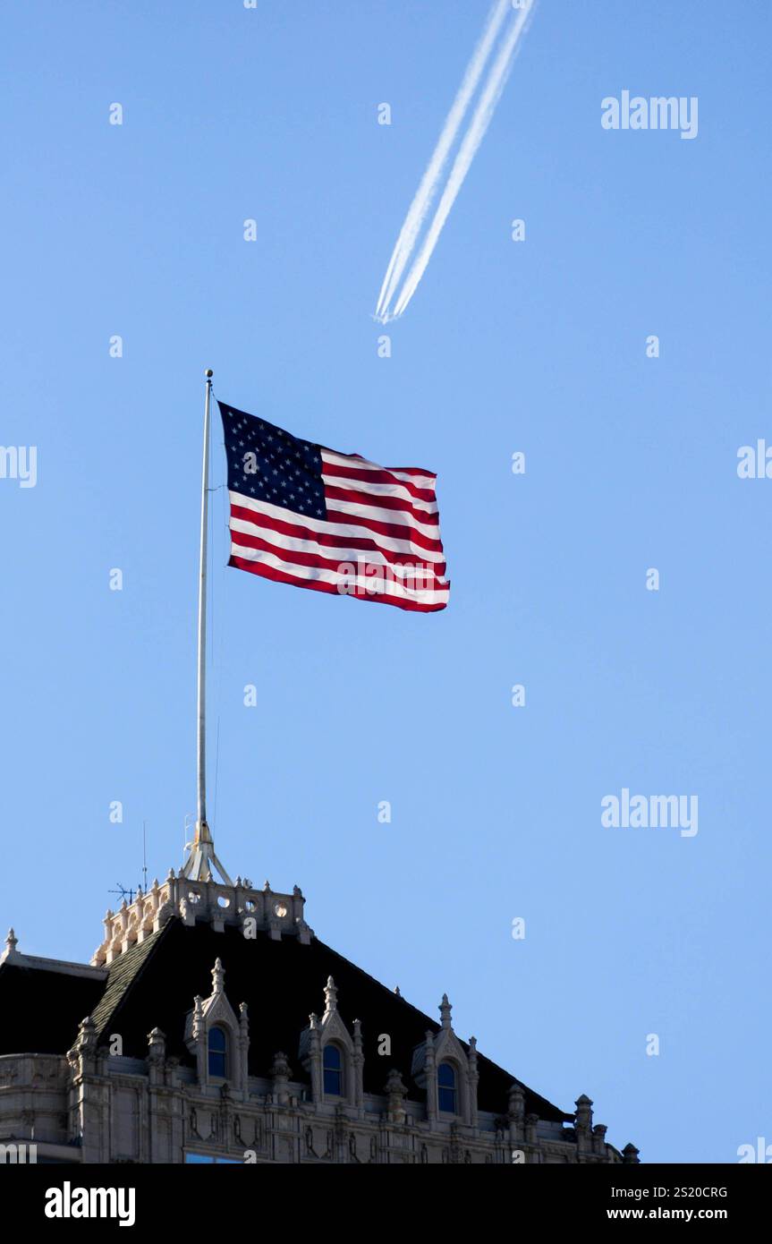 Plane with contrail above historic building and American flag waving ...