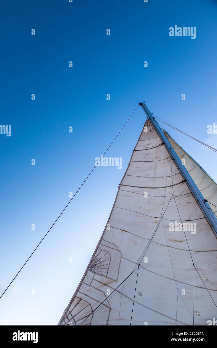 The elegance of a single sail reaching into a pristine blue sky, a ...