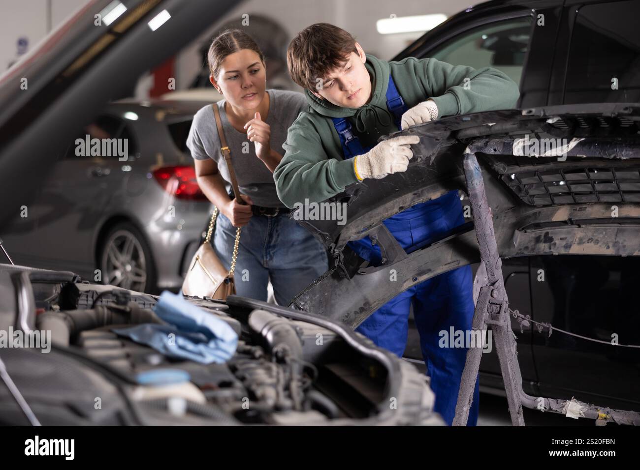 An auto mechanic shows a woman what problem is with her car bumper ...