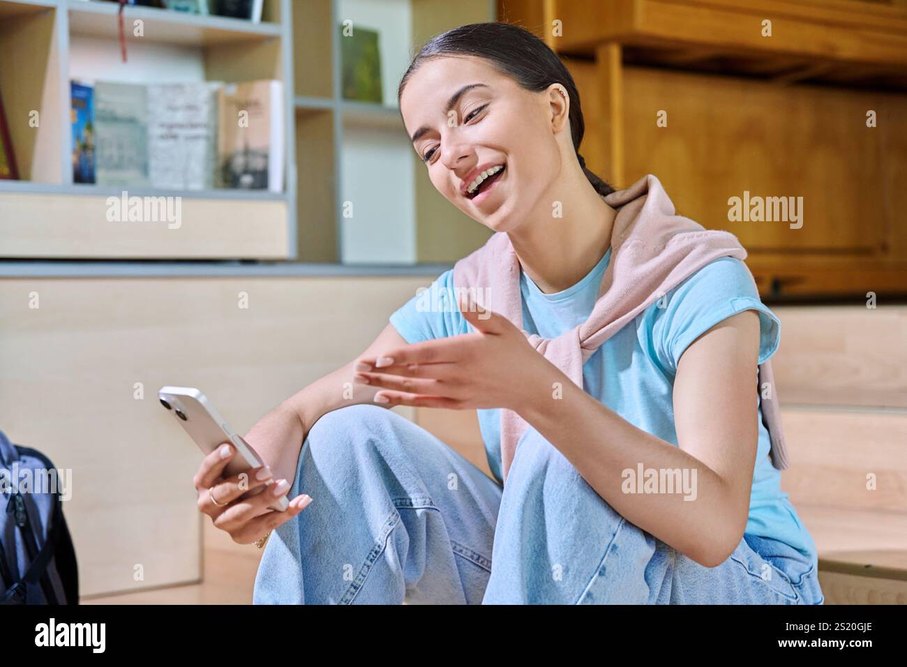 Teenage female student using smartphone, inside high school library ...