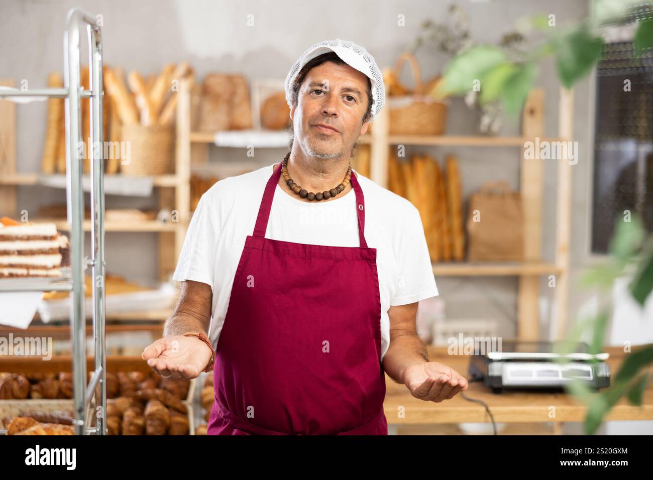Portrait of friendly baker selling fresh baguettes and croissants in ...
