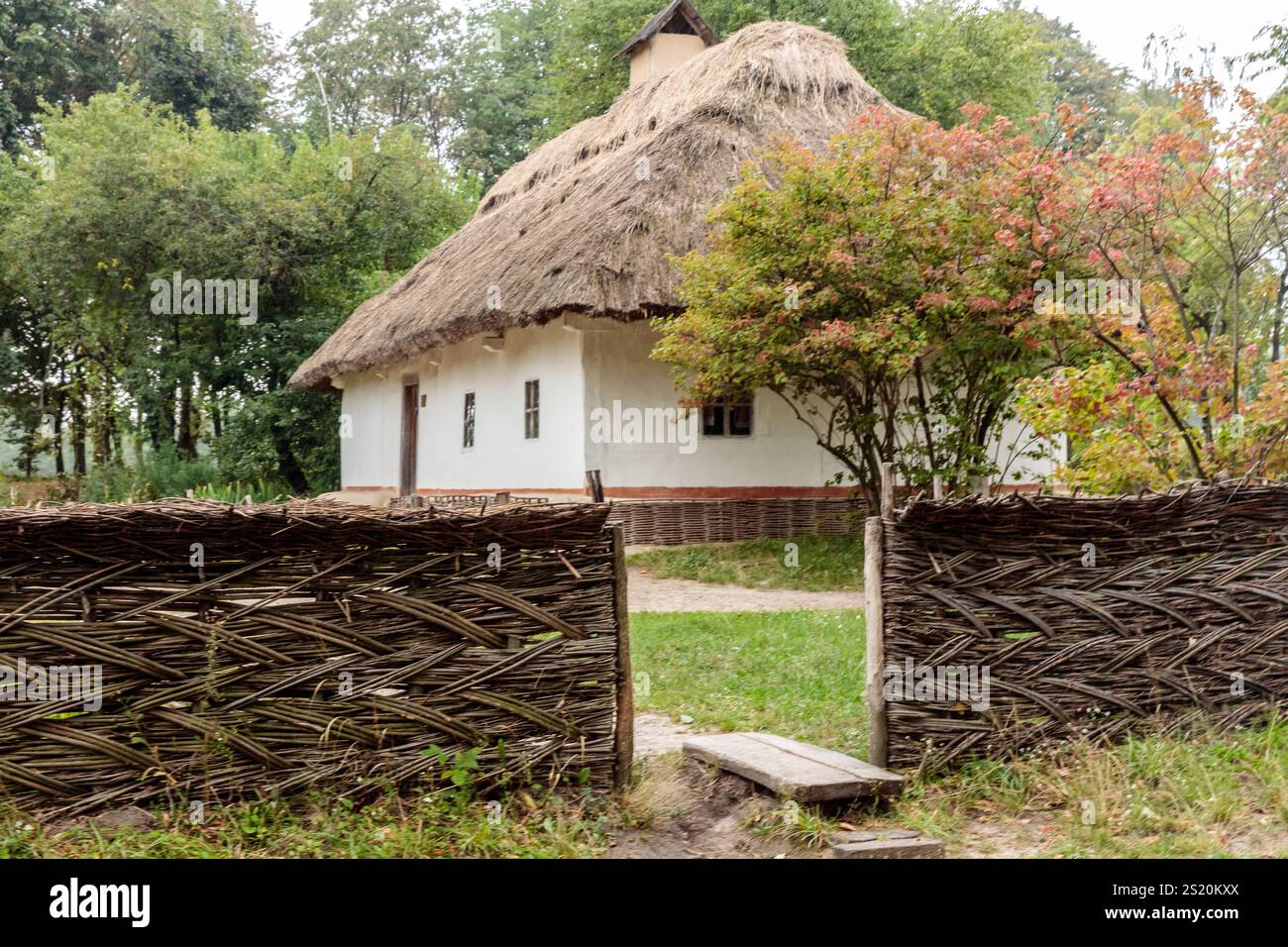 A small house with a thatched roof and a wooden fence. The house is ...