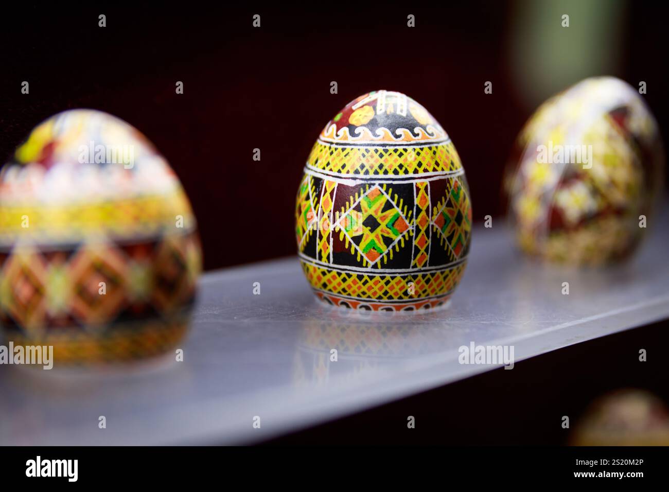 Three colorful eggs are displayed on a shelf. The eggs are decorated ...