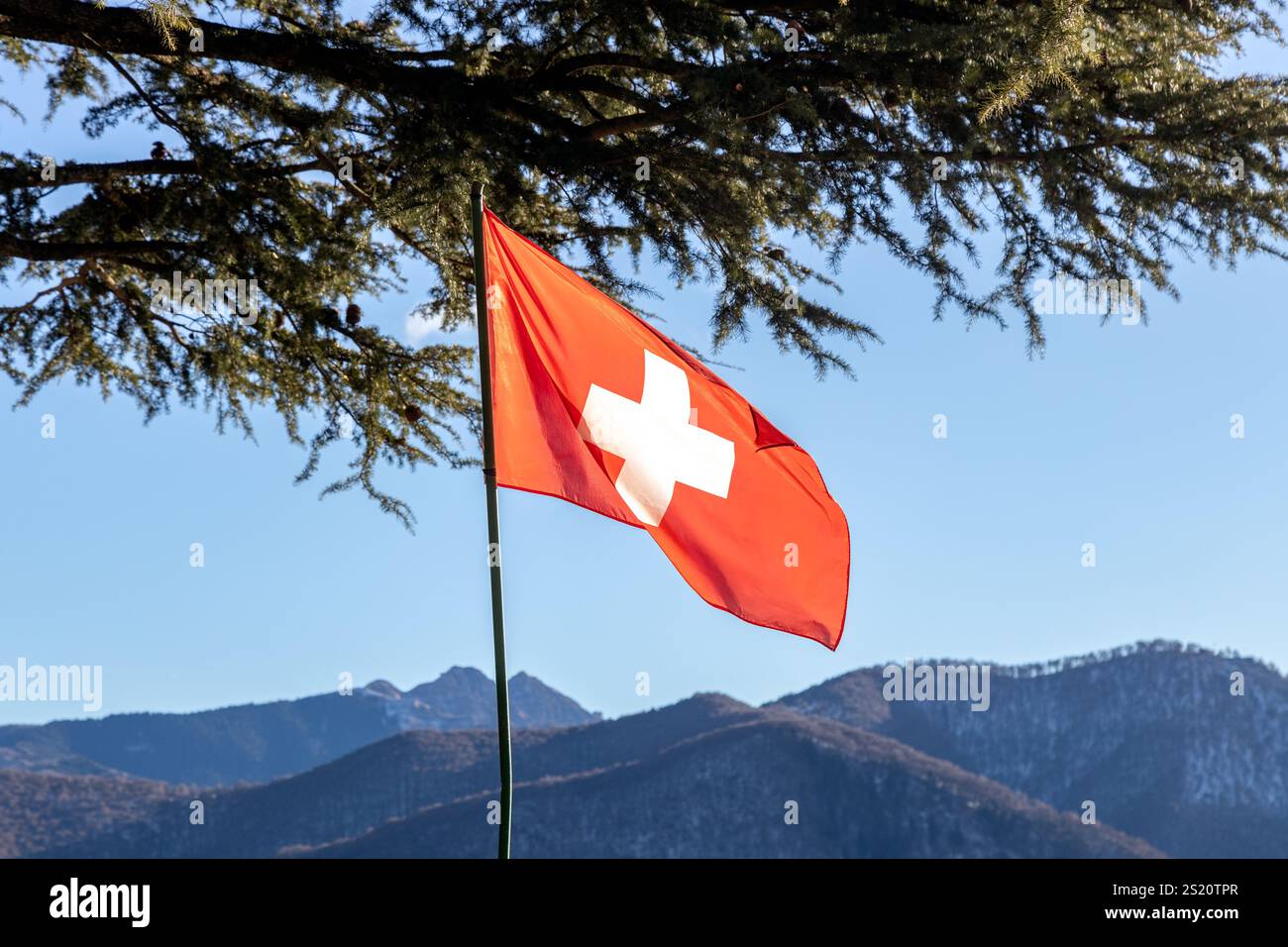 Swiss flag waving atop Monte Bre with mountains in the background ...