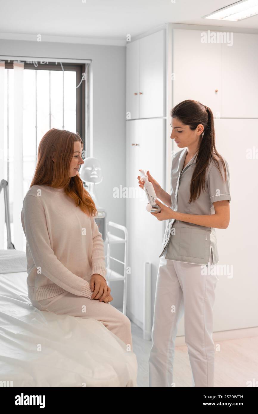 Female cosmetologist explaining skin care product to woman in clinic ...