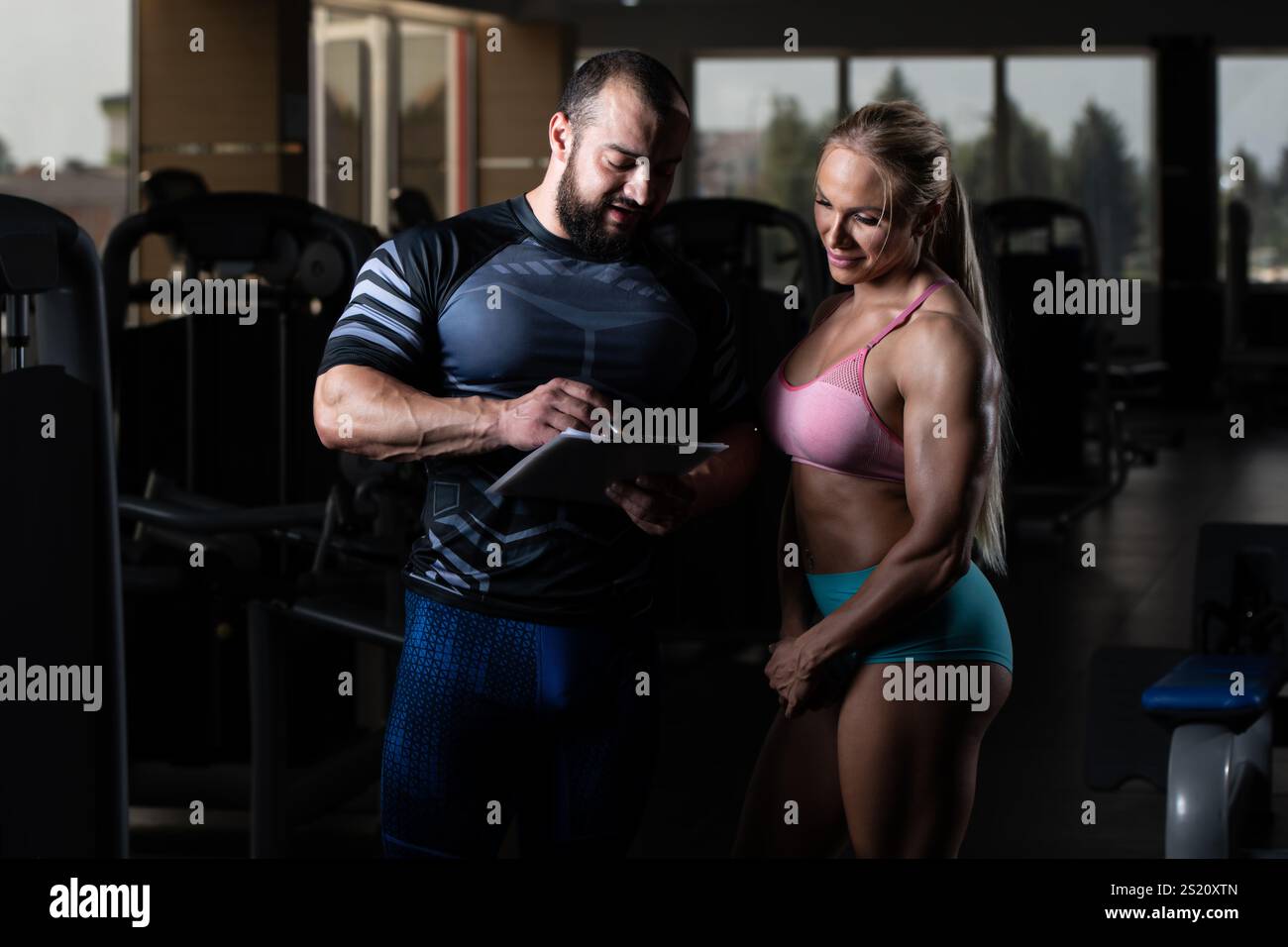 Male Trainer Giving Instructions To His Female Client While Noting Down The Details Of Her ...