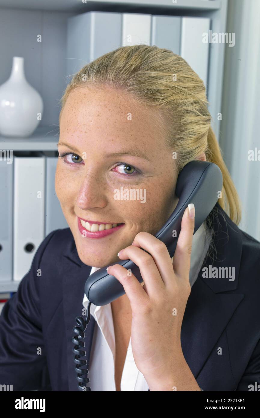 A friendly woman talks on the phone at her desk in the office and notes ...
