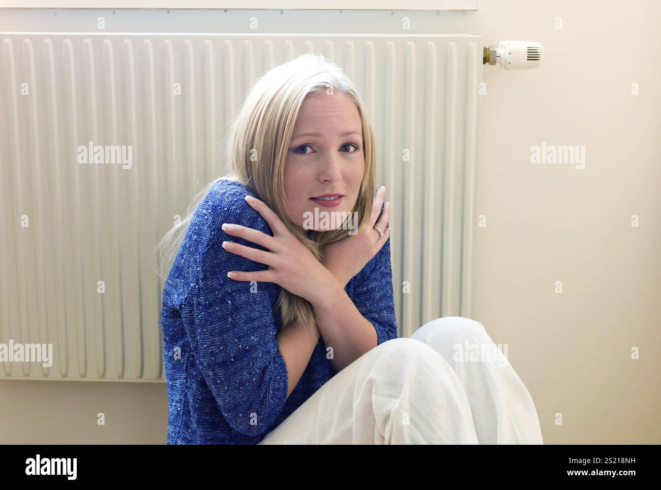 A young woman sits in front of a radiator and freezes. Rising heating ...