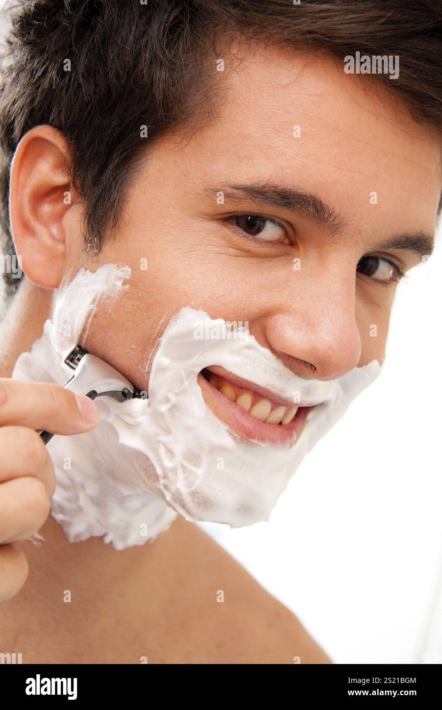 Young man shaves with razor blade and shaving foam in the bathroom ...