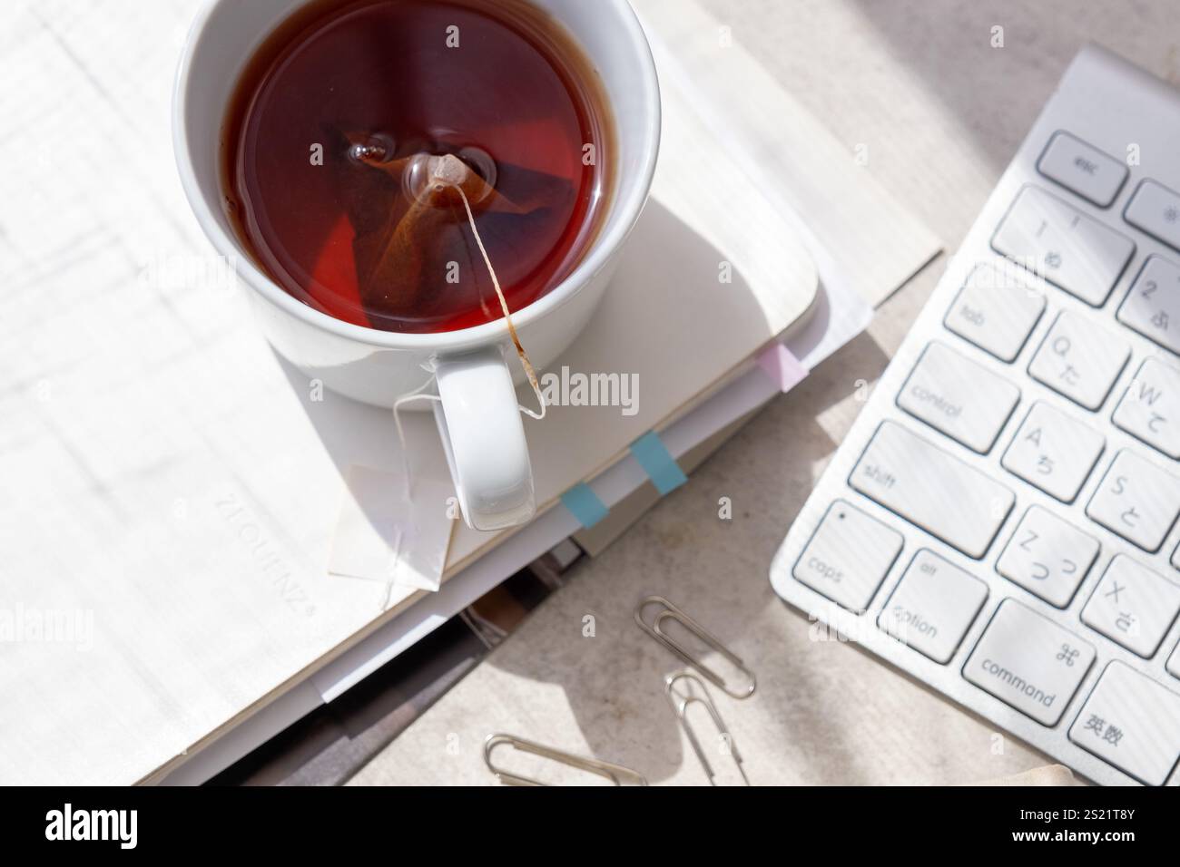 Keyboard, tea, notebook, documents and clips on a grey table by the ...