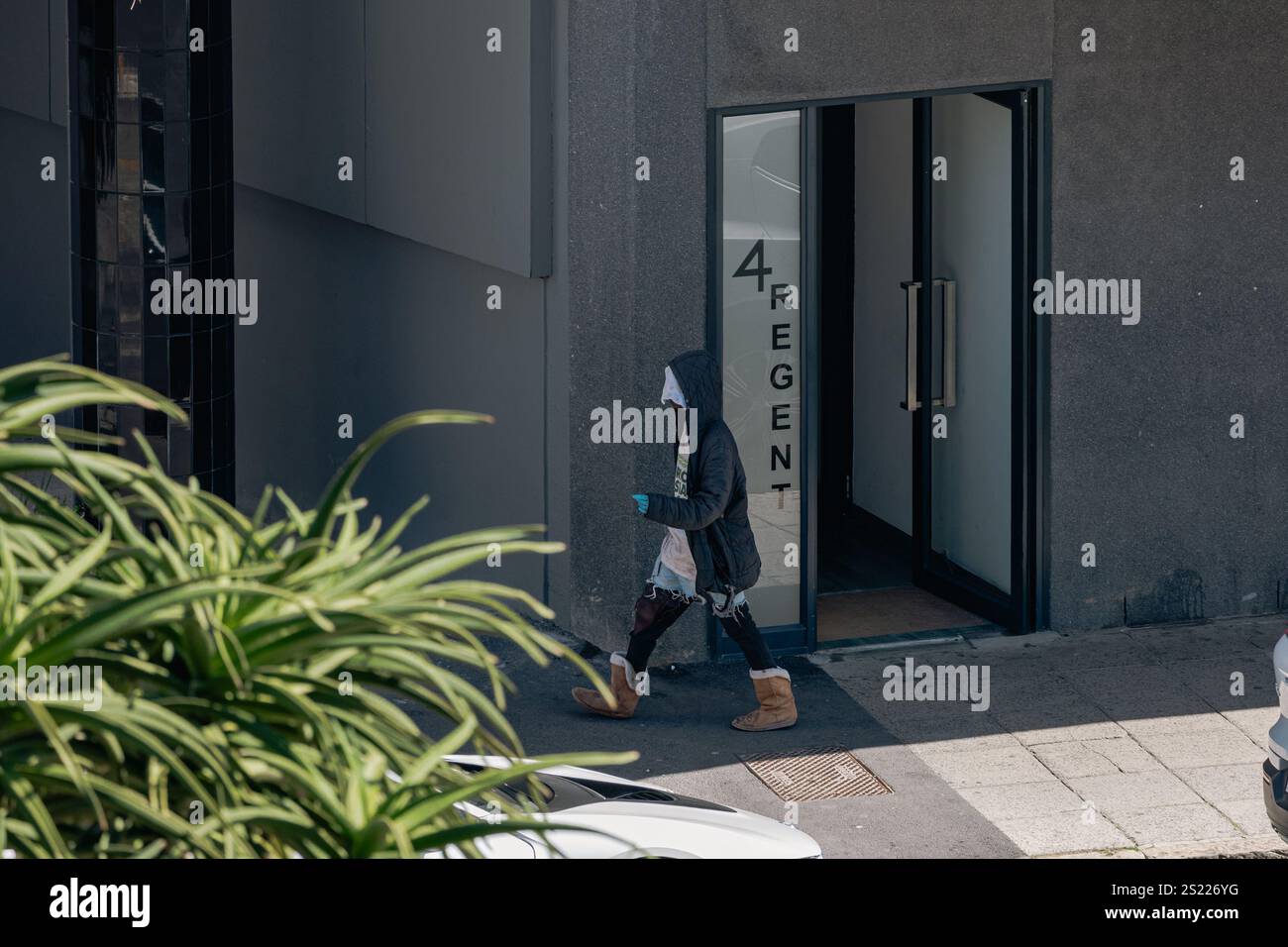 A homeless African man in strange clothing walks down the street, past ...