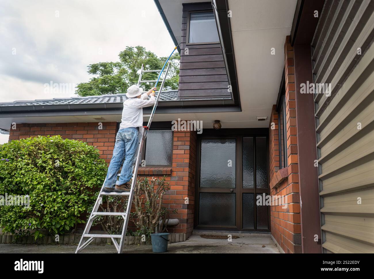 Man standing on the ladder and cleaning house with a long brush. Home ...
