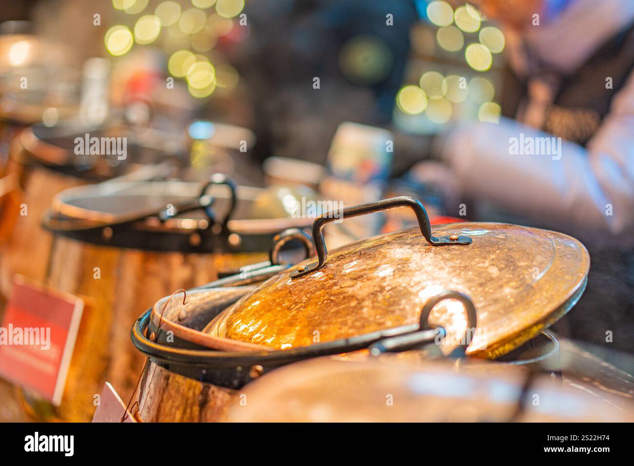 Image shows multiple copper-colored cooking pots arranged on an outdoor ...