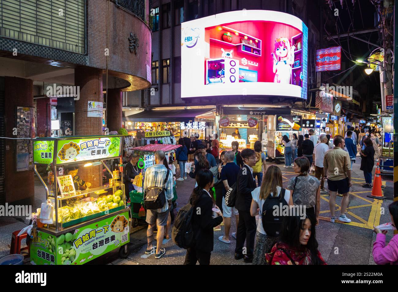 people enjoying a local street market at night in downtown Taipei in the Shilin district, where ...