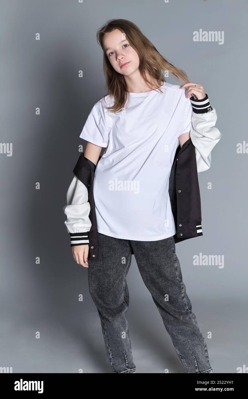 The young girl holds her jacket in a laid-back manner, eyes cast down ...