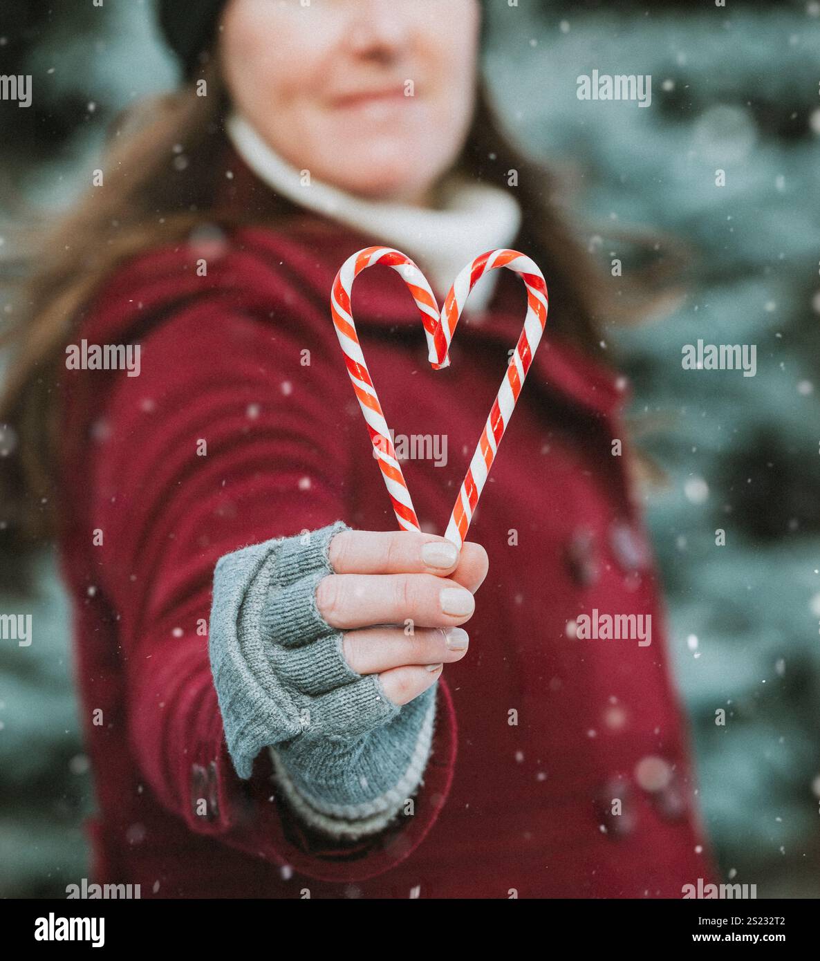 Crop of woman in red coat holding candy canes in heart shape in snow ...