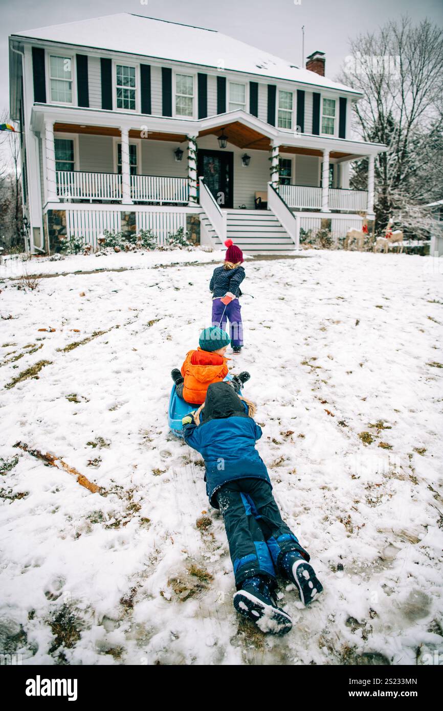 Kids pulling and riding sleds on a snowy lawn in front of a cozy home ...