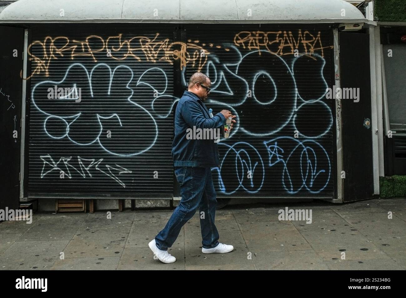A man walking past a closed shop with the security shutters covered in ...
