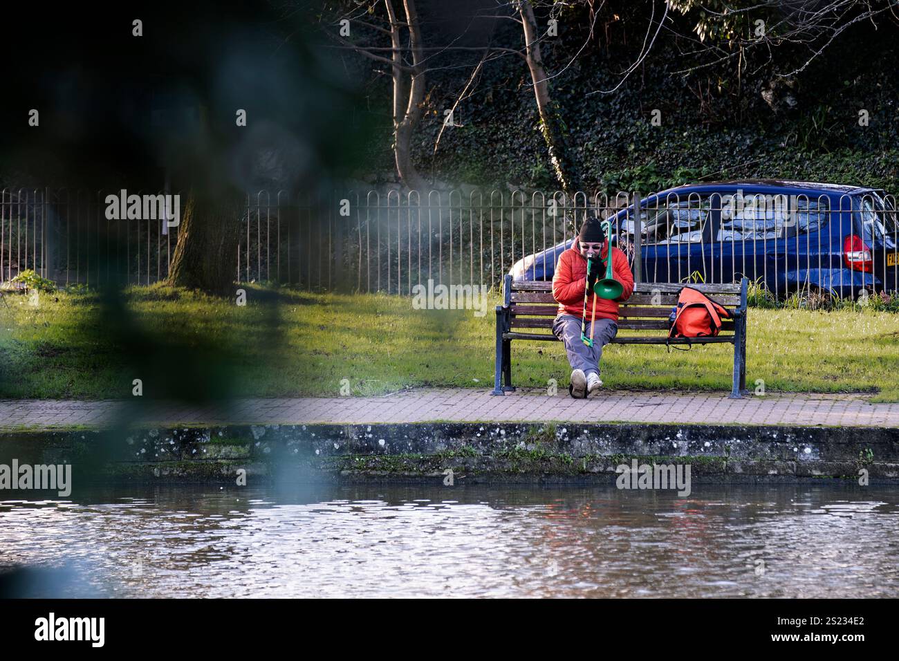 A man sitting on a bench by Trenance Boating Lake and playing the ...