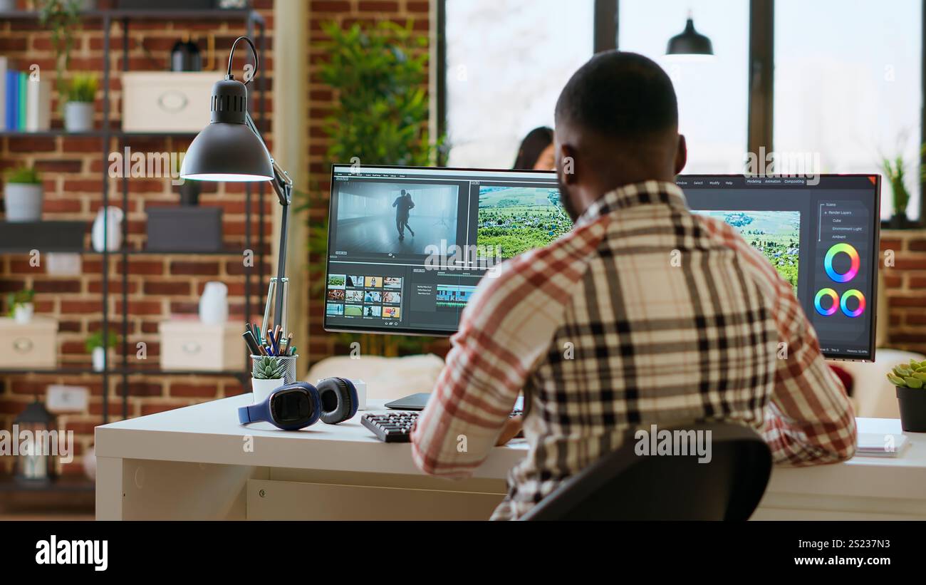 Male video editor works from modern home office in the living room, multitasking with a dual ...